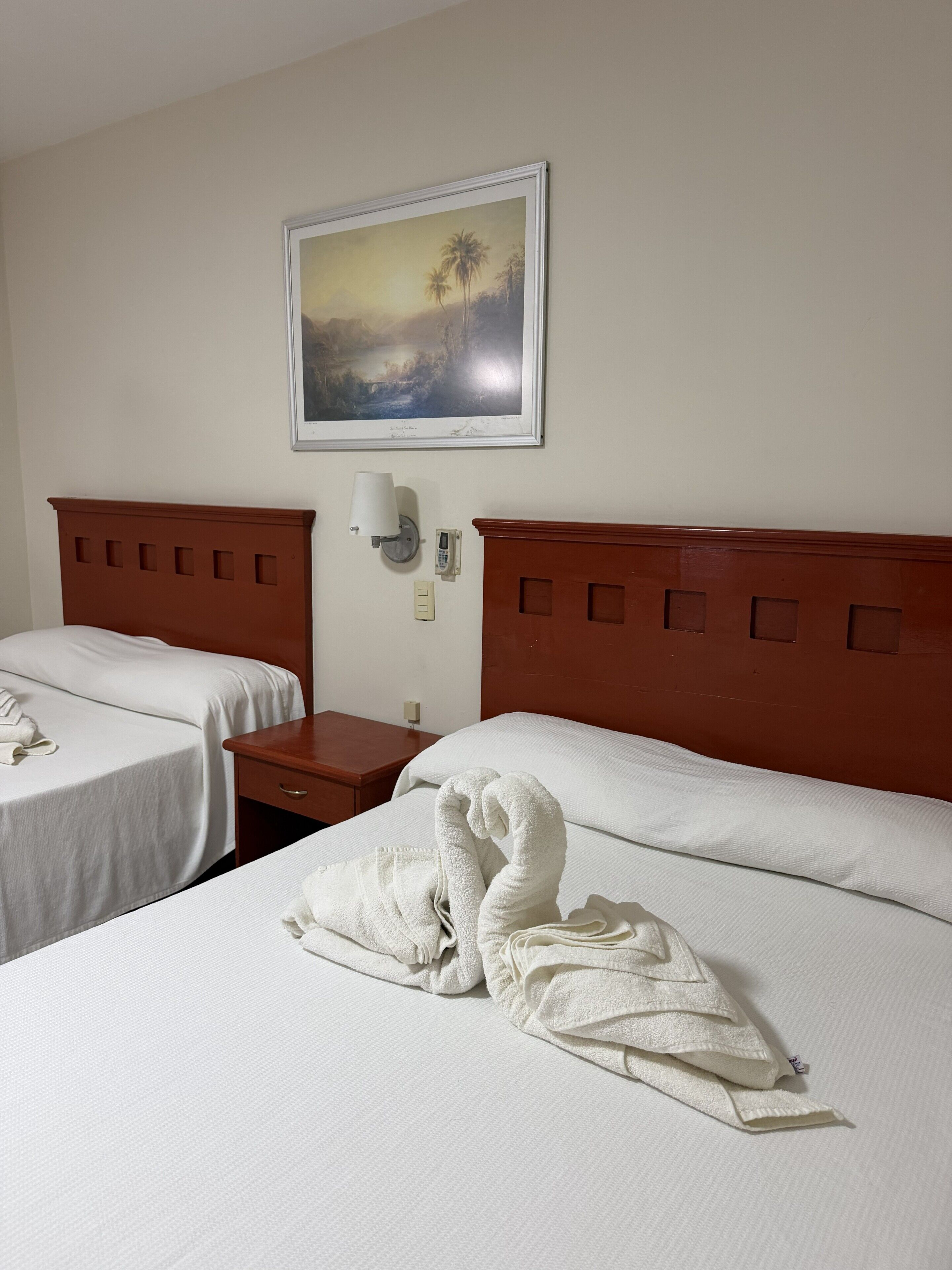 Quarto de hotel com duas camas, um quadro na parede, um abajur e um telefone.