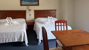 Quarto de hotel com duas camas, cabeceira de madeira, um quadro na parede, uma mesa de madeira e uma cadeira.