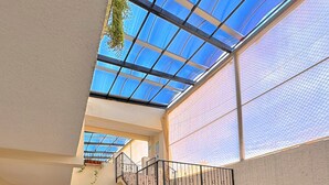 Um espaço interior com vários níveis, uma escadaria central, área de piscina e teto de vidro que permite a entrada de luz natural.