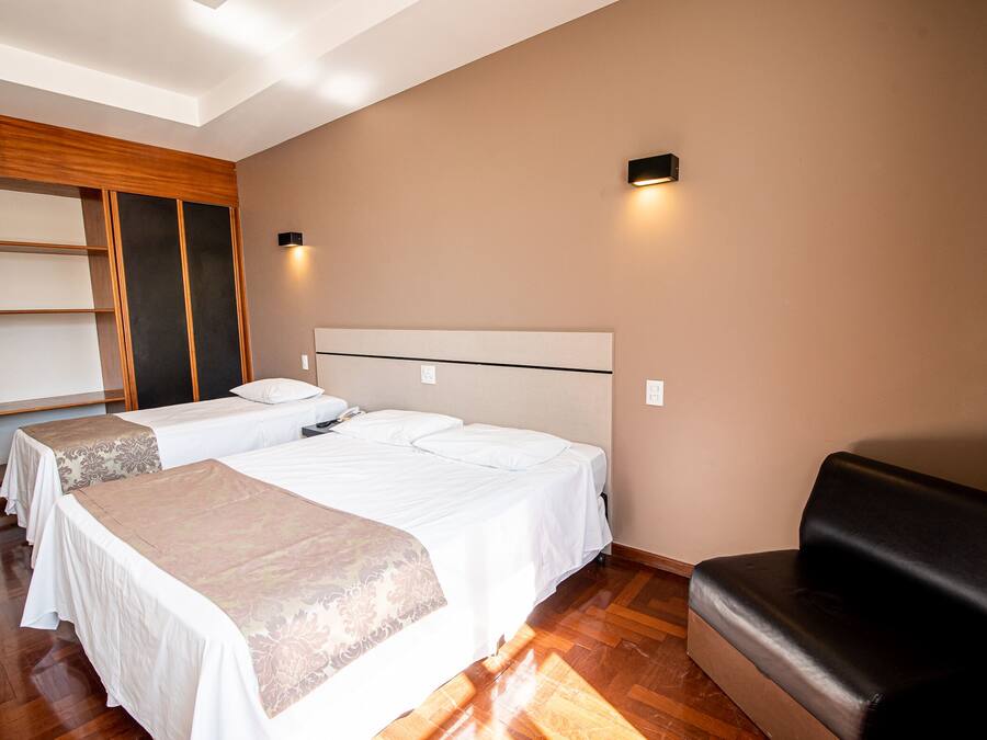 Quarto de hotel com duas camas, um sofá e um guarda-roupa de madeira.