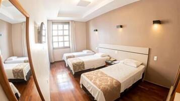 Quarto de hotel com três camas de solteiro, um espelho grande e uma janela com cortinas.
