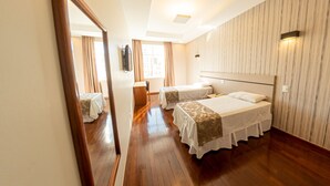 Quarto de hotel com duas camas, chão de madeira, espelho e televisão na parede.