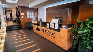 Bancada de recepção no Hotel Serrano, com vista clara para a área de recepção, uma escada para o andar superior e uma planta em vaso à direita.