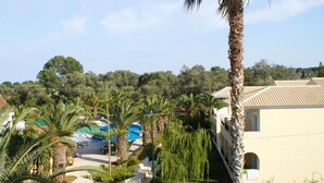 Um resort com área de piscina, palmeiras e um edifício com telhado de azulejos.