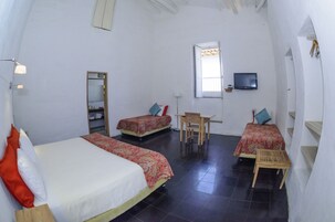Quarto com duas camas, uma escrivaninha, uma cadeira, uma TV e uma janela.