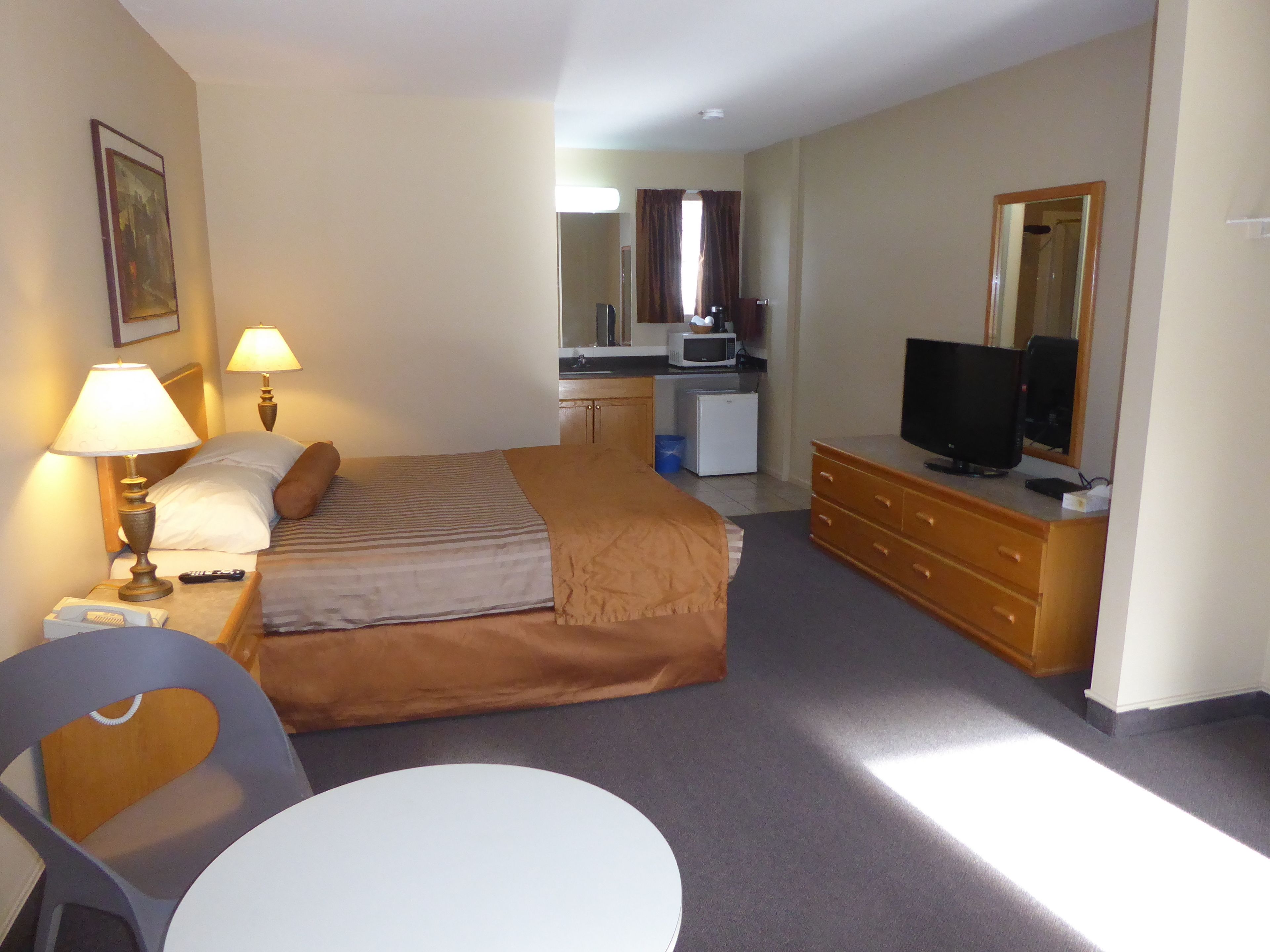 Quarto de hotel com cama, luminárias de cabeceira, televisão, escrivaninha com cadeira, pequena copa e espelho.