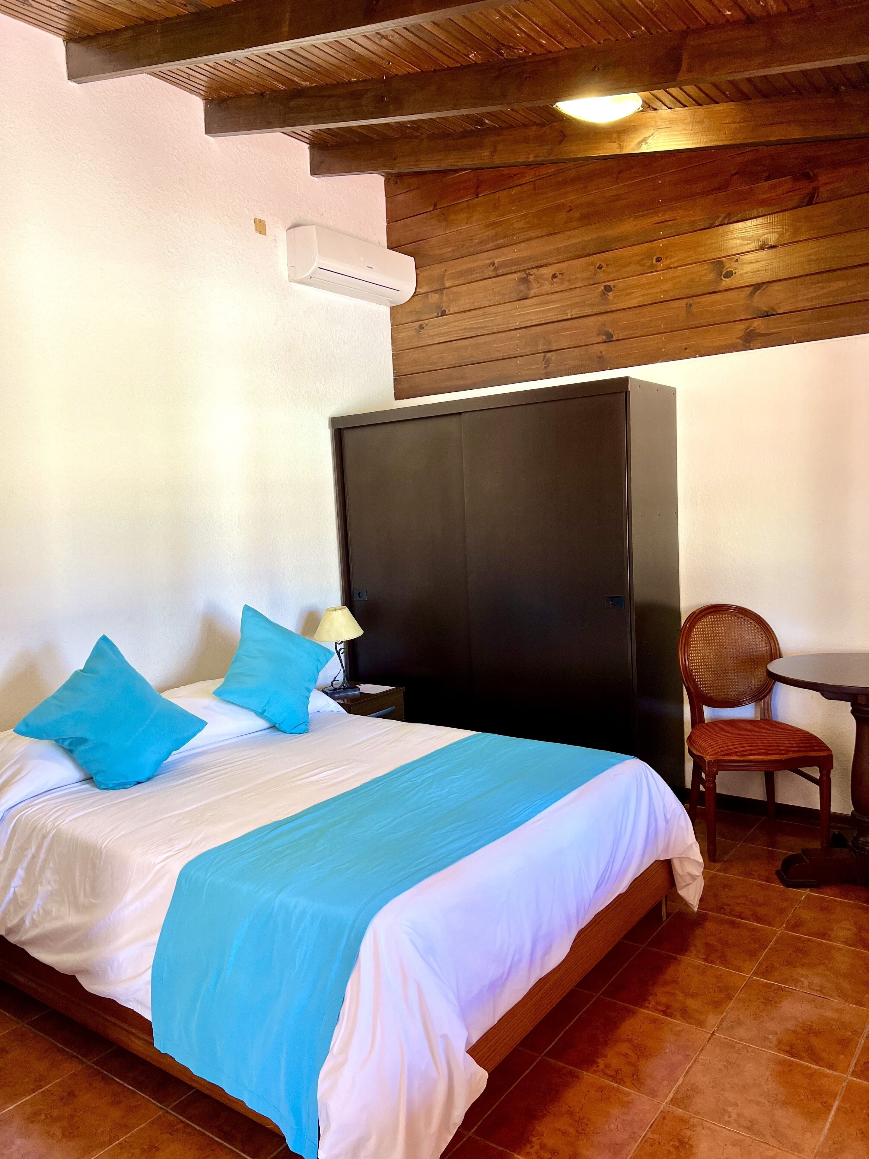 Um quarto com cama, guarda-roupa, cadeira e mesa.