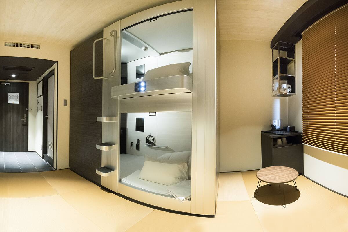 Quarto de hotel moderno com cama curva, estantes embutidas e uma pequena mesa redonda.