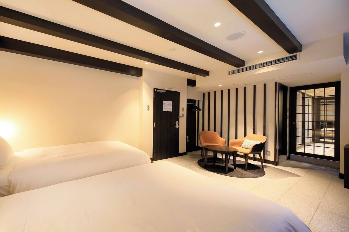 Quarto de hotel com uma cama grande, um espaço de estar com duas cadeiras e vista através de uma porta de vidro.