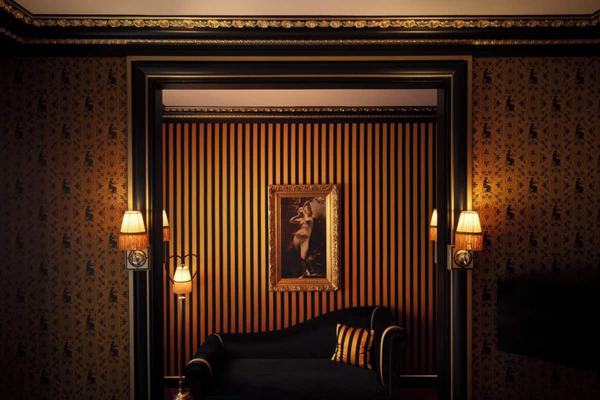 Um quarto com um sofá escuro, um quadro na parede e duas luminárias fixadas.