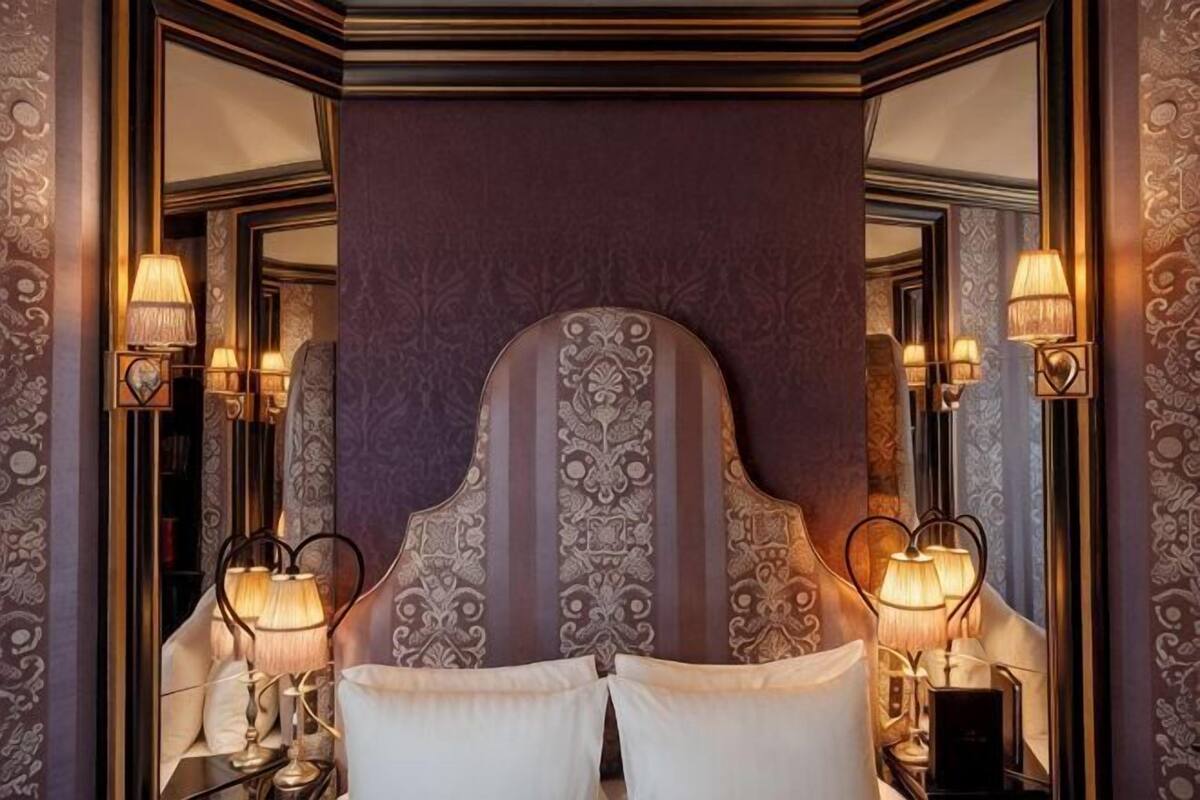Uma cama com cabeceira decorativa, duas luminárias de apoio e um espelho sobre a cama.