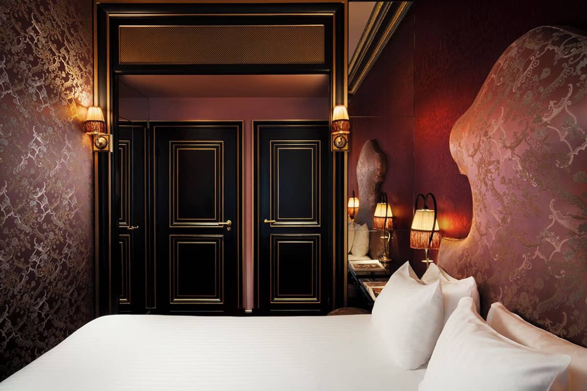 Quarto de hotel com uma cama grande, duas portas e luminárias fixadas na parede.