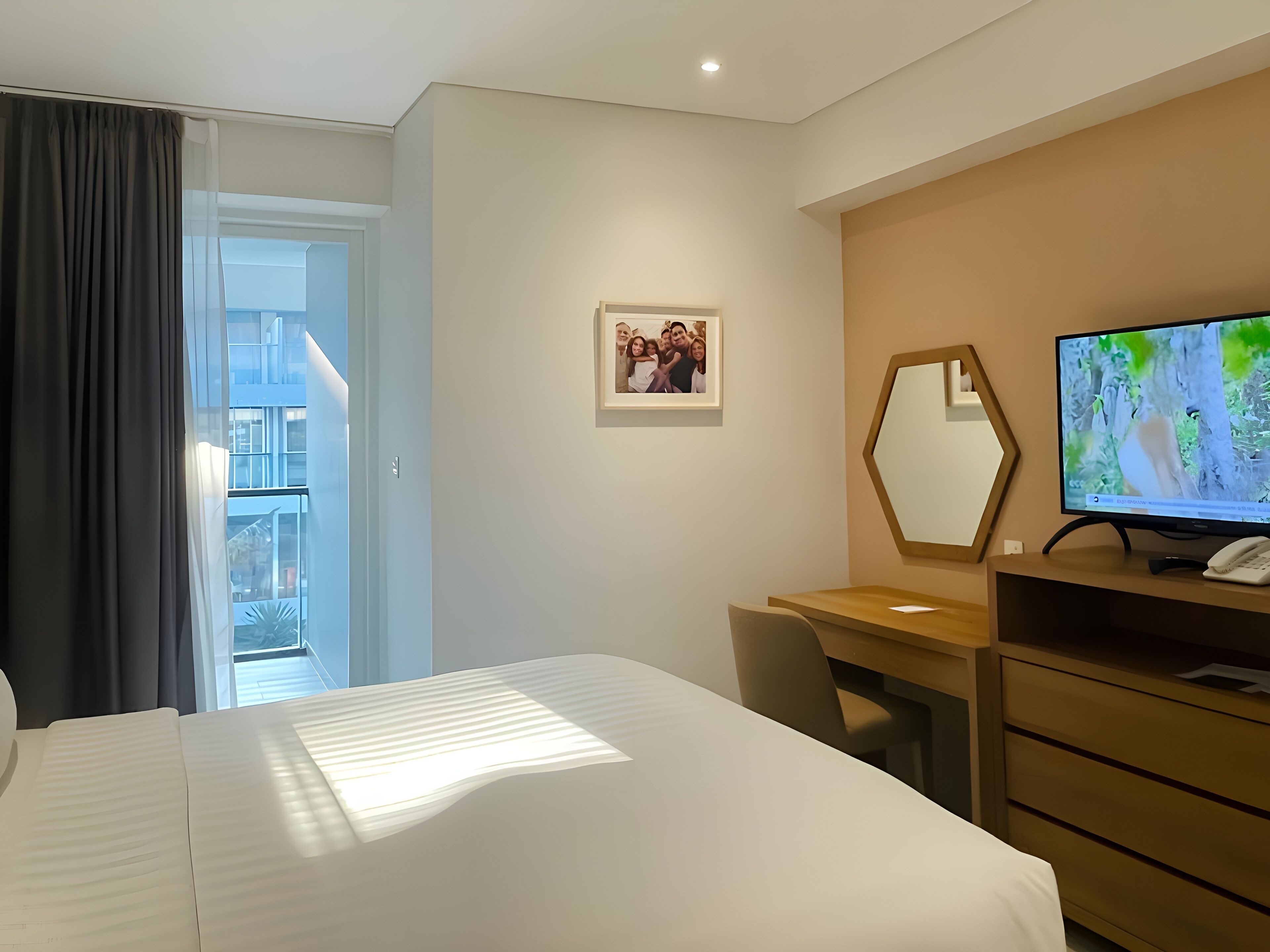 Quarto de hotel com uma cama, escrivaninha, televisão e um quadro na parede.