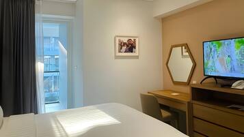 Quarto de hotel com uma cama, escrivaninha, televisão e um quadro na parede.