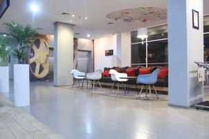 Um hall moderno com um grande mural de relógio, um balcão de recepção e uma área de estar com um sofá vermelho e cadeiras brancas.