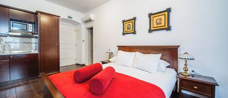 Quarto de hotel com cama, mesa de cabeceira, luminária, micro-ondas e cozinha.
