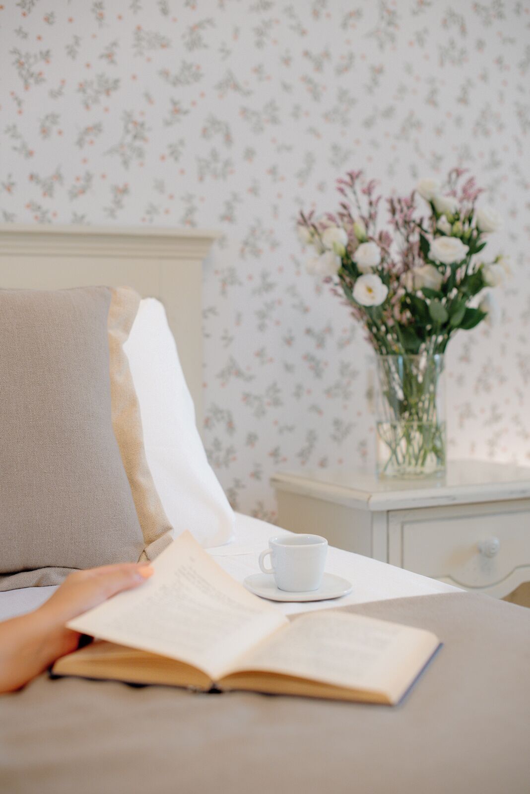 Uma cama com travesseiro, uma xícara de chá e um livro sobre a mesa de cabeceira.
