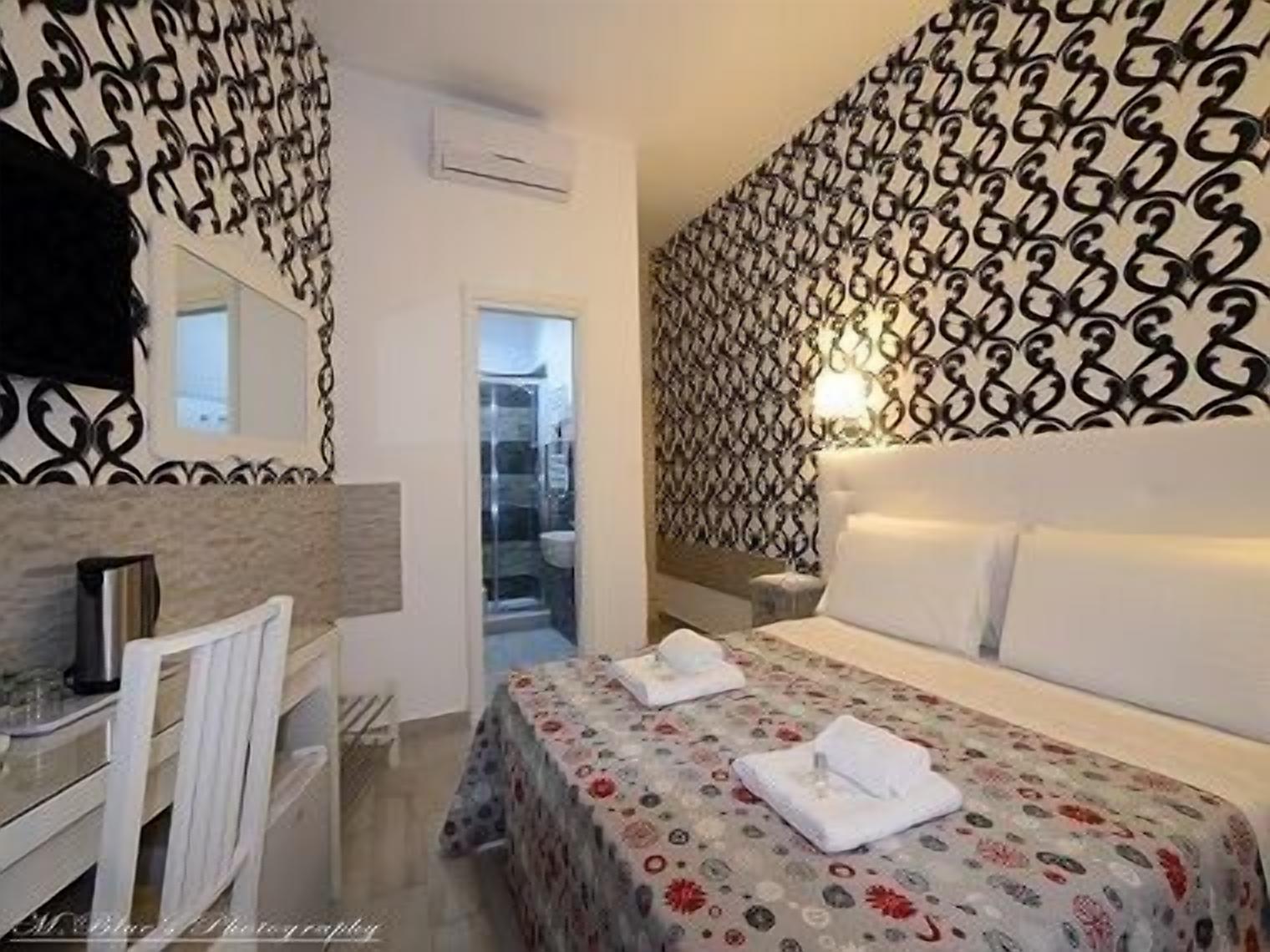 Quarto de hotel com cama, escrivaninha e chuveiro.