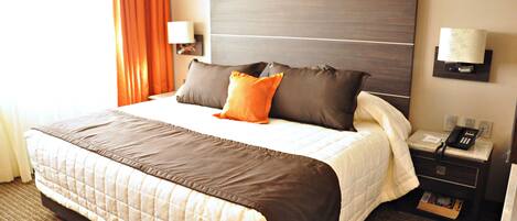 Quarto de hotel com uma cama grande, duas luminárias de cabeceira, mesa de cabeceira com telefone e piso coberto de carpete.
