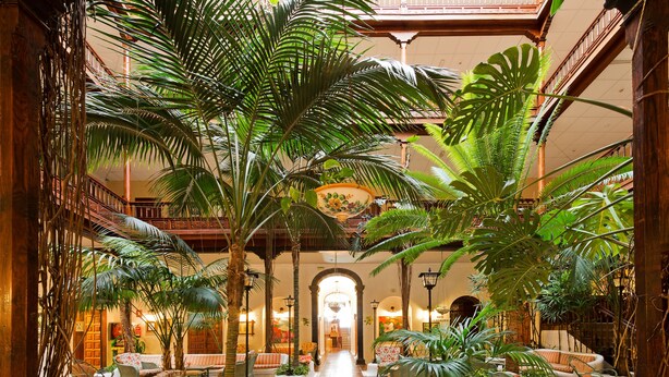 Um amplo átrio interno com uma passarela central aberta, rodeado por áreas de estar e plantas tropicais exuberantes.