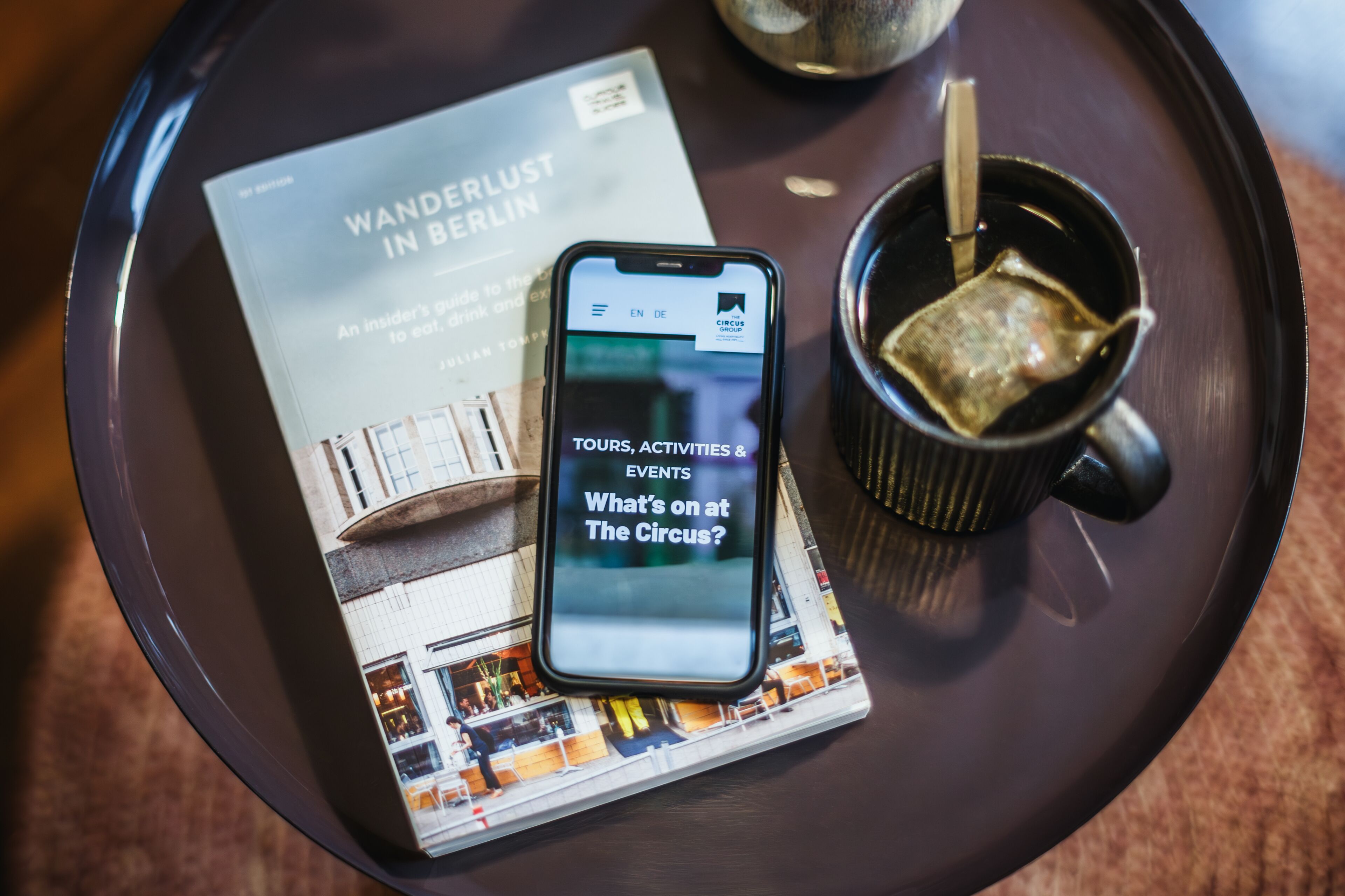 Um smartphone exibindo um aplicativo de viagens sobre uma bandeja com uma revista e uma xícara.