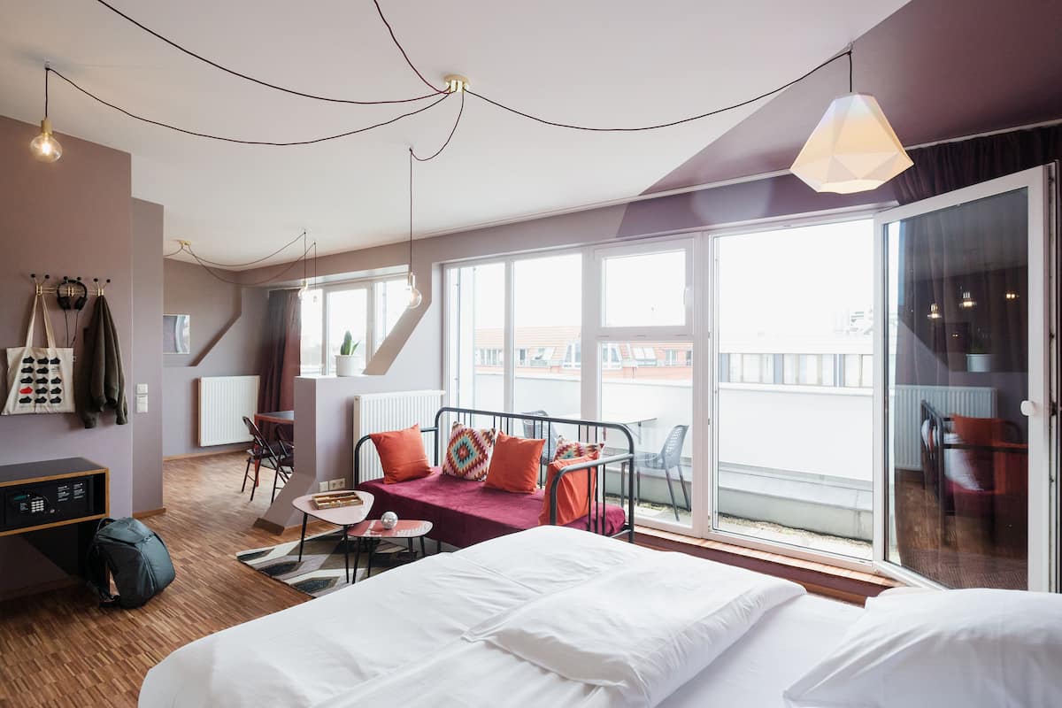Quarto de hotel moderno com uma cama grande, uma escrivaninha, uma cadeira e uma varanda com vista.