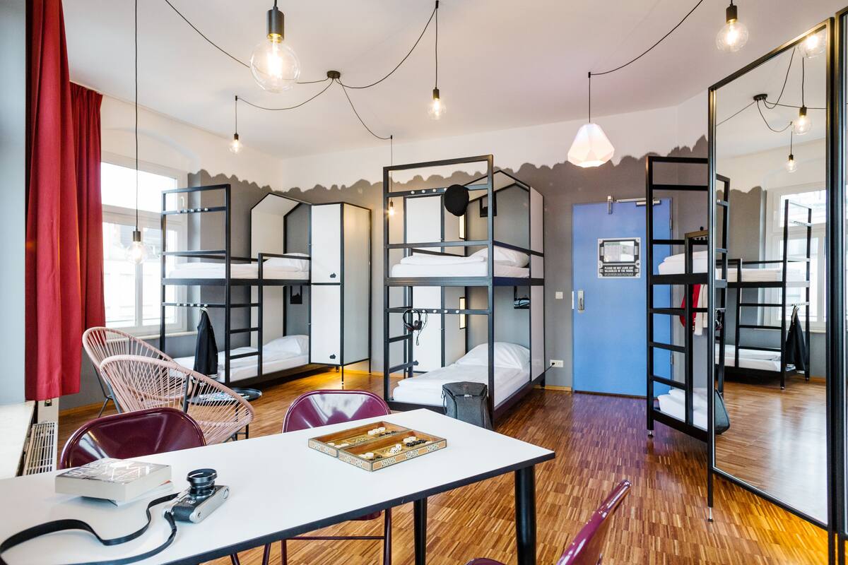 Quarto de hotel moderno com beliches, mesa de jantar e espelho.