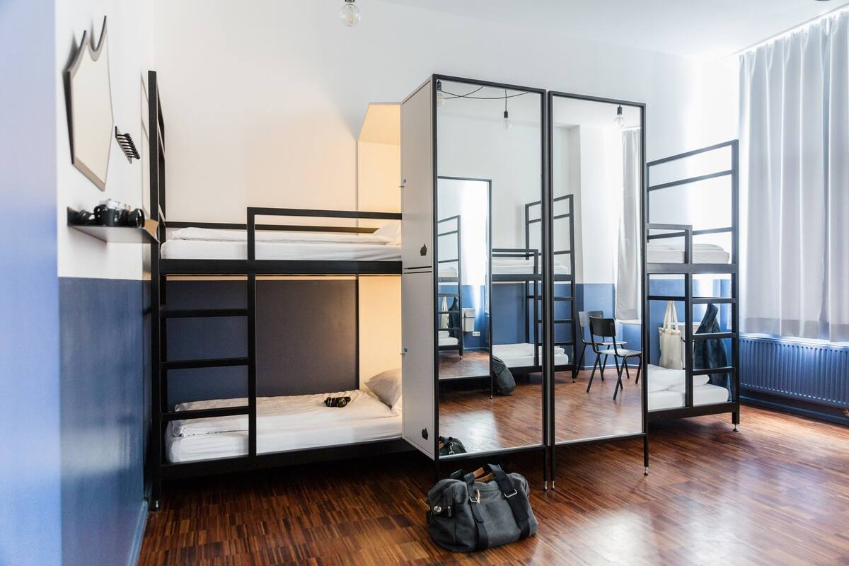 Quarto de hotel moderno com beliche, guarda-roupa com espelho, escrivaninha e cadeira.