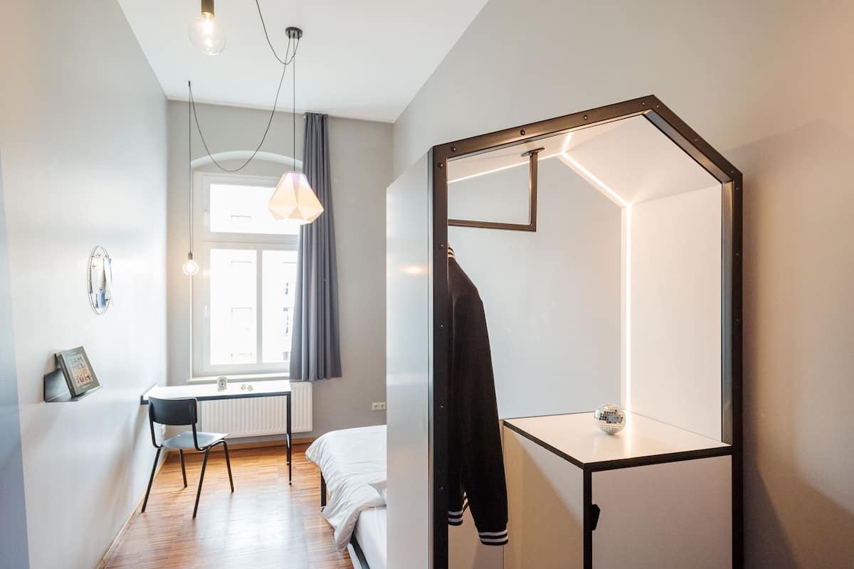 Quarto de hotel moderno com uma cama, escrivaninha, cadeira, espelho e luminária pendente.