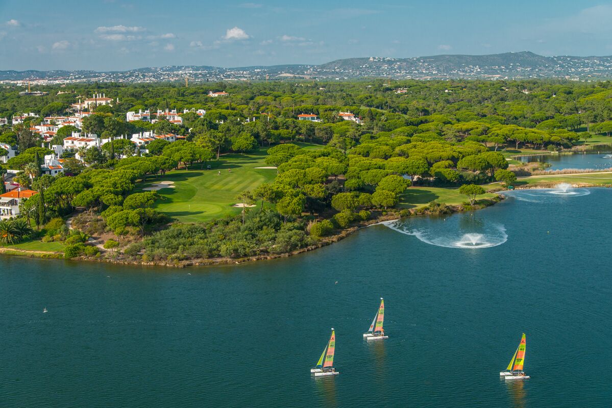 Uma área costeira com um campo de golfe, barcos a vela e um lago.