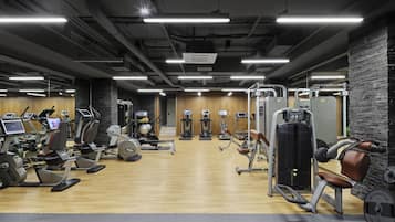 Uma academia com diversos equipamentos de exercício, piso de madeira e uma parede de destaque em pedra.