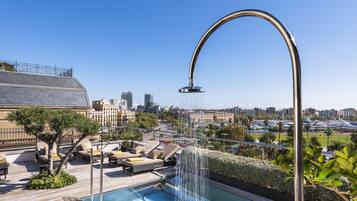 Piscina no terraço com chuveiro em cascata, espreguiçadeiras e vista para a cidade.