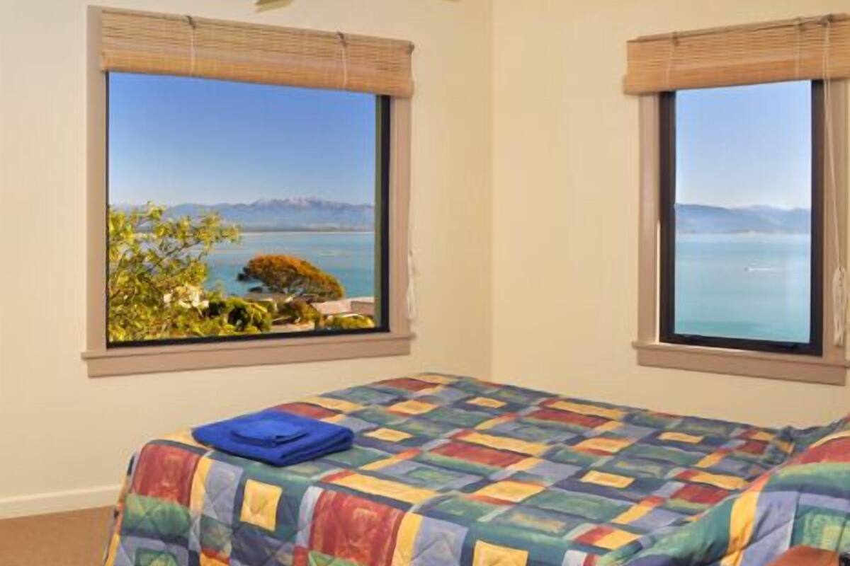 Quarto com duas janelas que oferecem vista para um lago e montanhas.