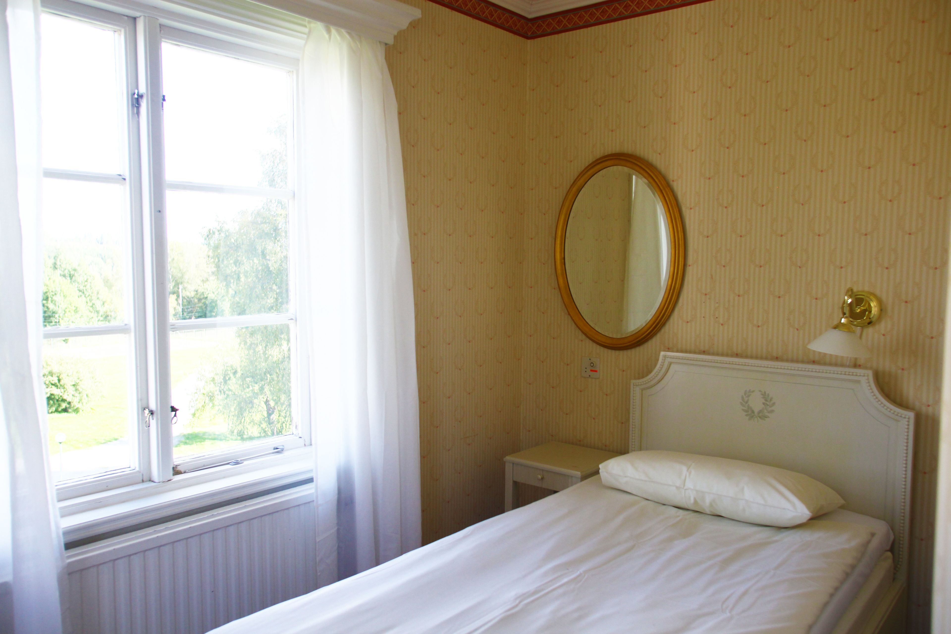 Quarto de hotel com uma cama, mesa de cabeceira, espelho e janela com cortinas.