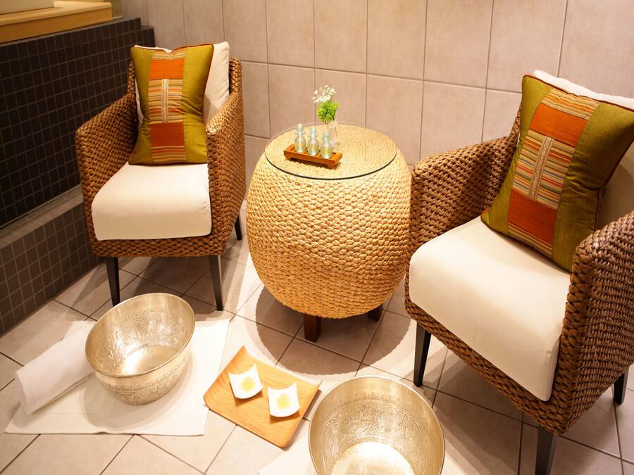 Uma área de estar com cadeiras de vime e uma mesa trançada, acompanhada por duas tigelas e um tabuleiro com uma garrafa e um copo.