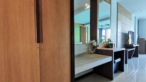 Quarto de hotel moderno com porta de madeira, um espelho grande, secador de cabelo, televisão e uma planta.