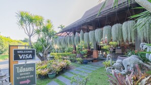 Entrada do resort com placa de boas-vindas, plantas em vasos e área de estar ao ar livre.
