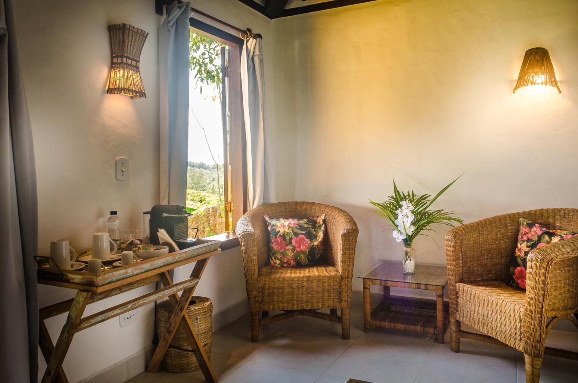 Quarto aconchegante com móveis de vime, uma mesa pequena e uma janela com cortinas.