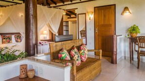 Um quarto aconchegante com um sofá de vime, cama com roupa de cama florida, televisão e um espaço de refeições com mesa e cadeiras.