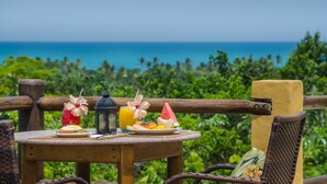Uma mesa de madeira com vista tropical, uma cadeira de vime e um corrimão de madeira.