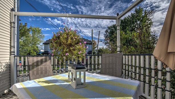 Um alpendre coberto com mesa e cadeiras, um arranjo de flores e vista para o bairro.