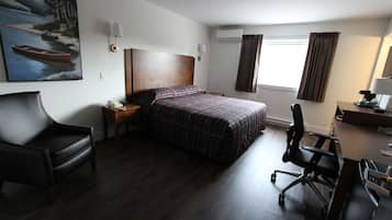 Quarto de hotel com cama, escrivaninha, cadeira, mesa de cabeceira, abajur e um quadro na parede.