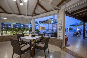 Uma área de varanda ao ar livre com móveis de vime, uma mesa com vela e vista para o mar.