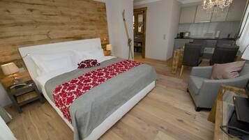 Quarto com cama grande, mesa de cabeceira com abajur, cabeceira de madeira e sofá cinza com almofada.