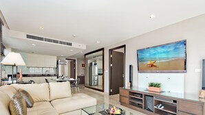 Uma sala de estar moderna com uma mesa de centro de vidro, um sofá bege e uma grande TV de tela plana na parede.