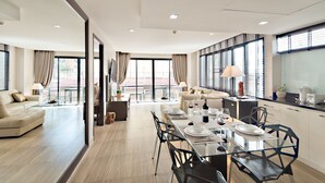 Quarto de hotel moderno com área de refeições, sofá e uma janela grande com persianas.