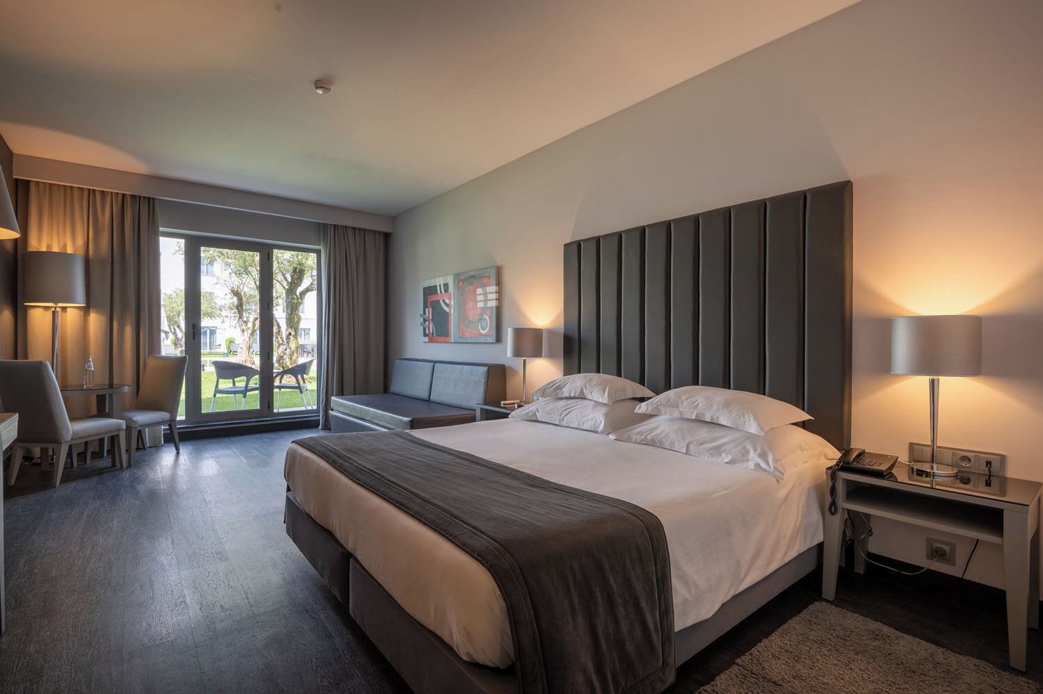 Quarto de hotel moderno com uma cama grande, uma escrivaninha, uma cadeira e vista para o exterior.