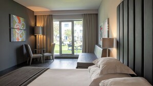 Quarto de hotel com cama, escrivaninha, cadeira, luminária e vista para o exterior.