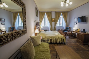 Quarto de hotel com uma cama grande, escrivaninha, cadeira, televisão e espelho.