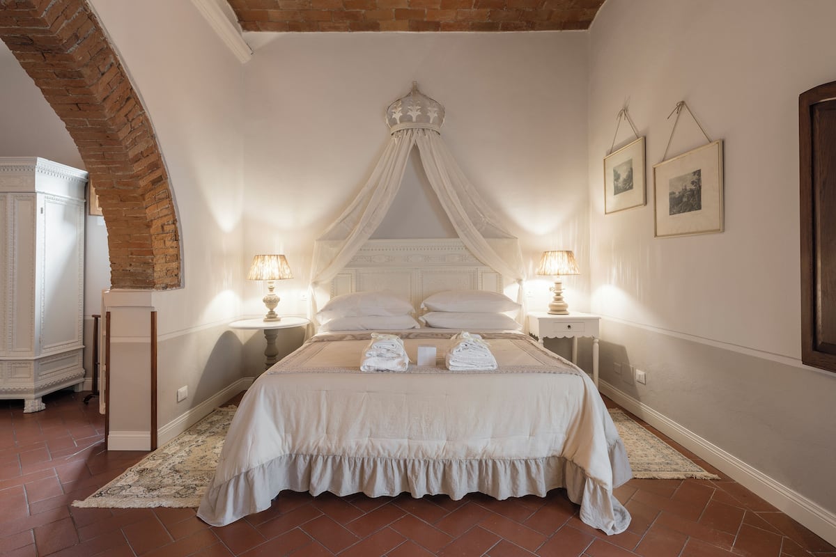 Quarto com cama de dossel, cortina e duas luminárias de cabeceira.